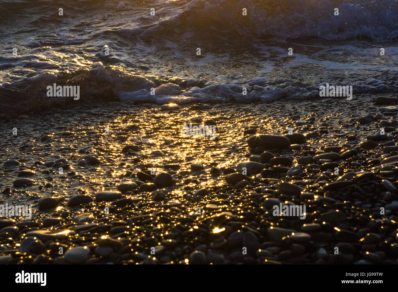 sea pebble beach with multicoloured stones, transparent waves with foam ...