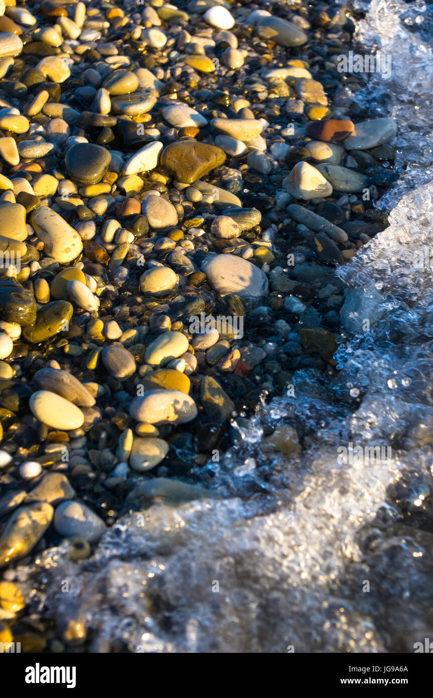 sea pebble beach with multicoloured stones, transparent waves with foam ...