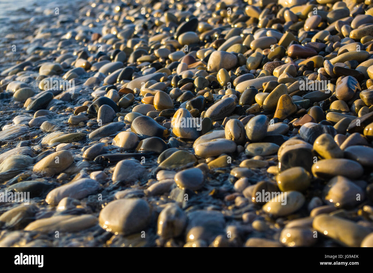 sea pebble beach with multicoloured stones, transparent waves with foam ...