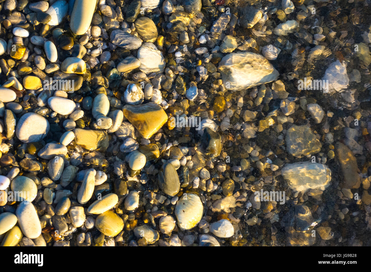 sea pebble beach with multicoloured stones, transparent waves with foam ...