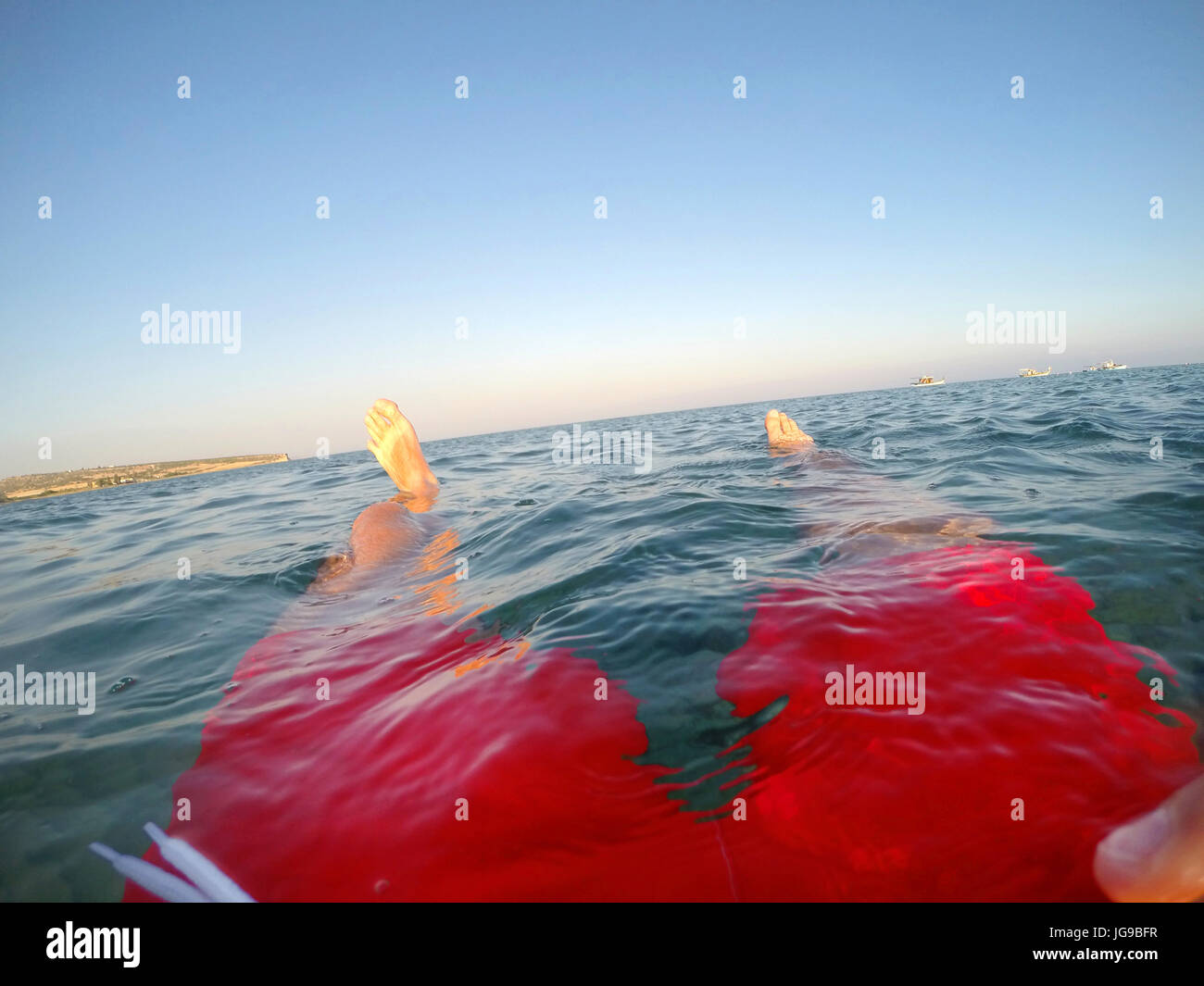 Man floating on sea water. Feet and legs of a swimmer in red swimwear ...
