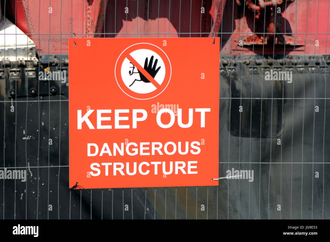 Sign on wire fence saying "Keep Out Dangerous Structure" with hand icon ...