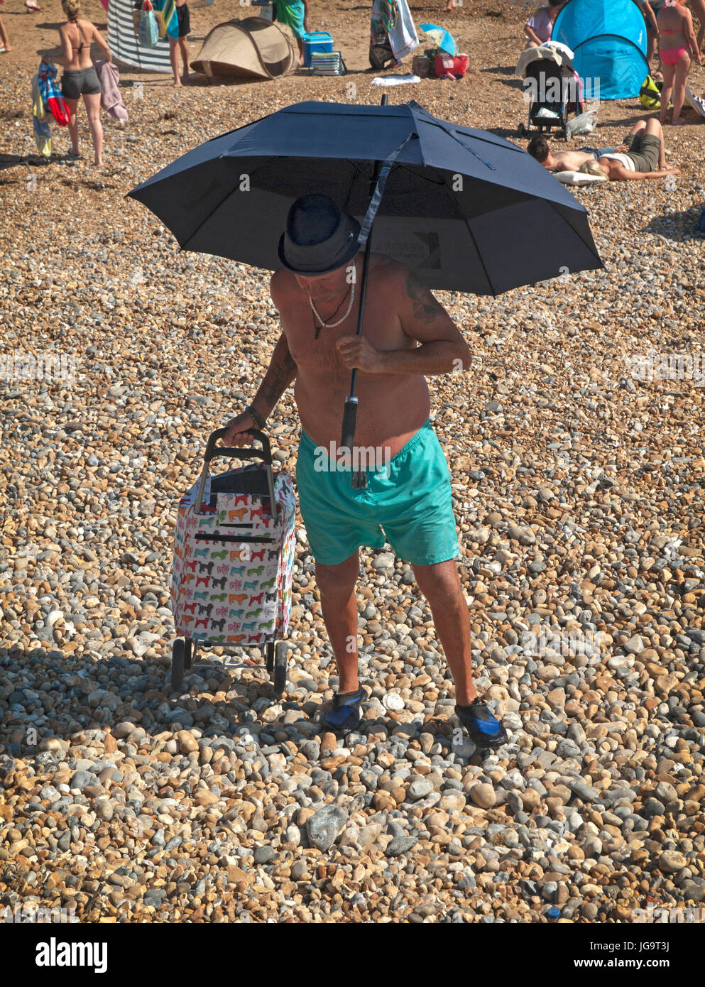 On a hot Brighton beach a man finds shade with his umbrella Stock Photo ...
