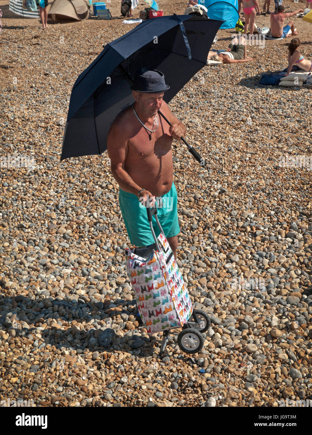 On a hot Brighton beach a man finds shade with his umbrella Stock Photo ...