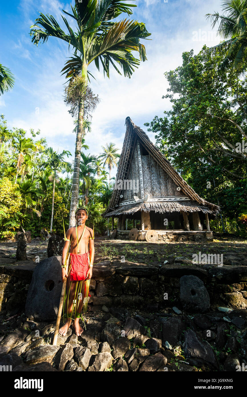 Young boy in traditional dress standing before a traditional hut on the ...