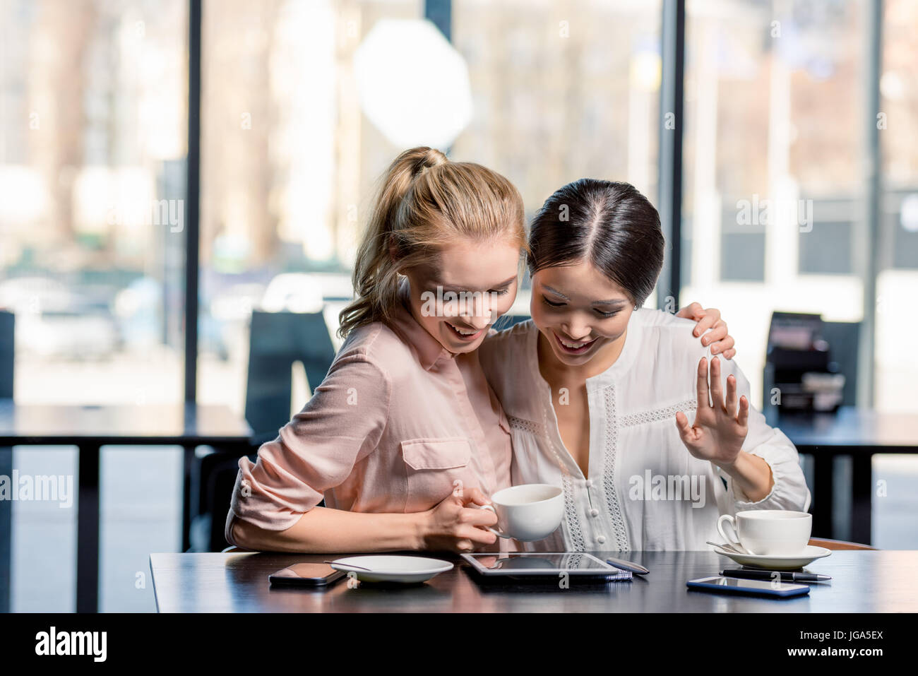 Smiling young women using digital tablet while drinking coffee in cafe ...