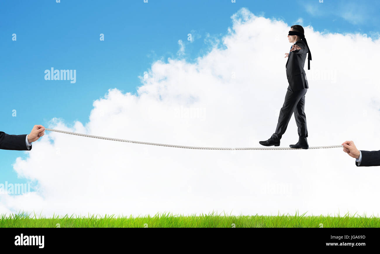 Businessman with blindfolder on eyes walking on rope over natural ...