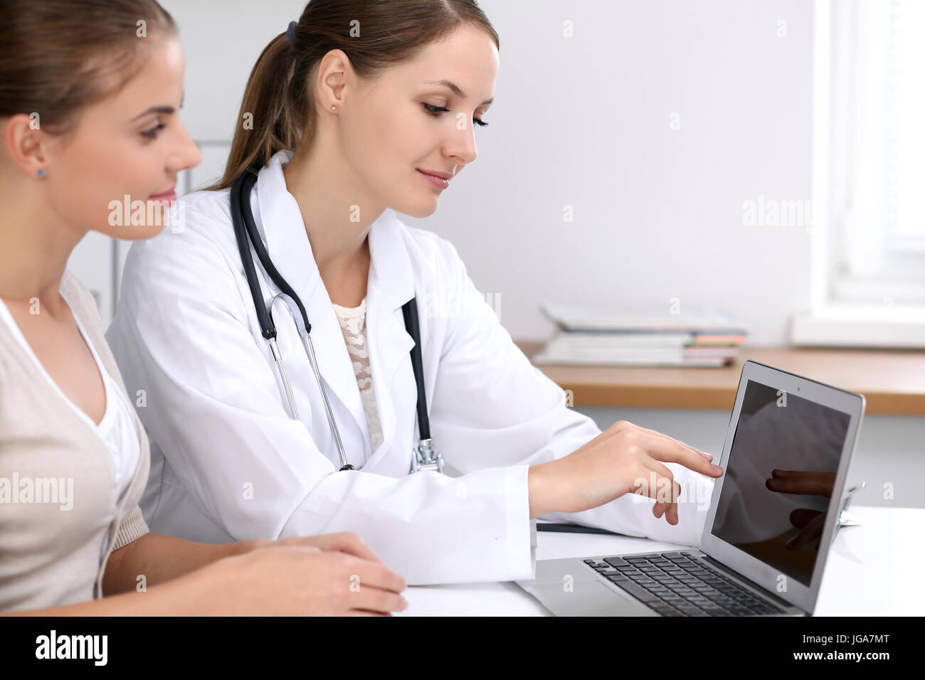 Doctor and patient sitting at the desk. Physician pointing into laptop ...