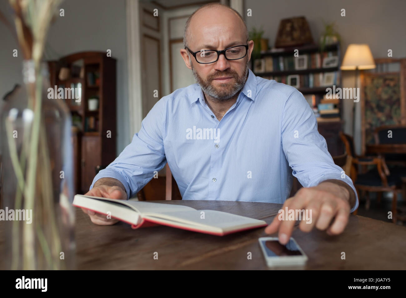 Man reading book indoor and using phone Stock Photo - Alamy