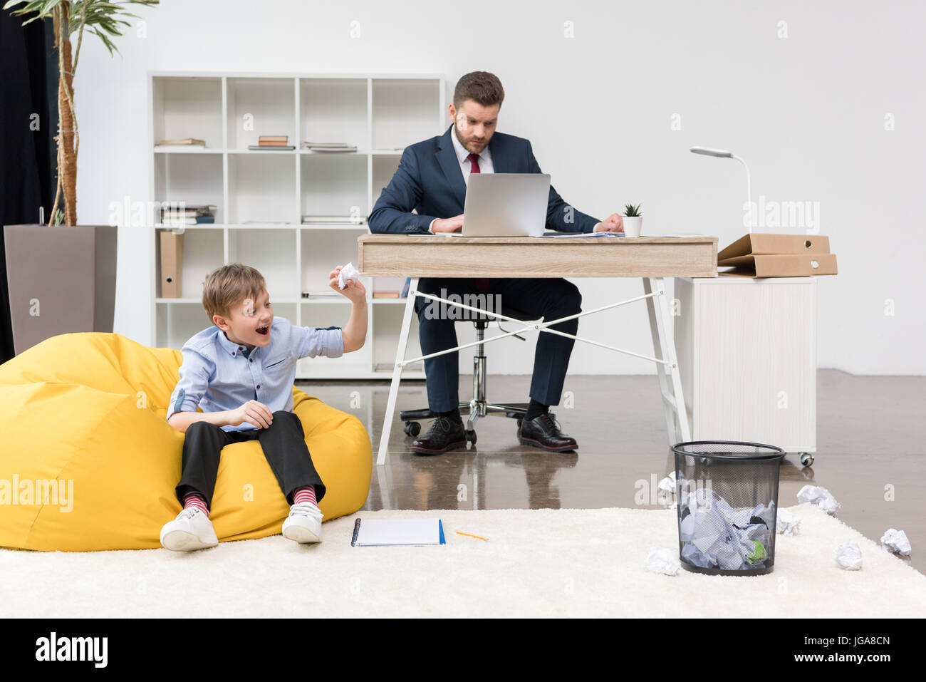 Happy boy playing trashketball while his father working at office Stock ...