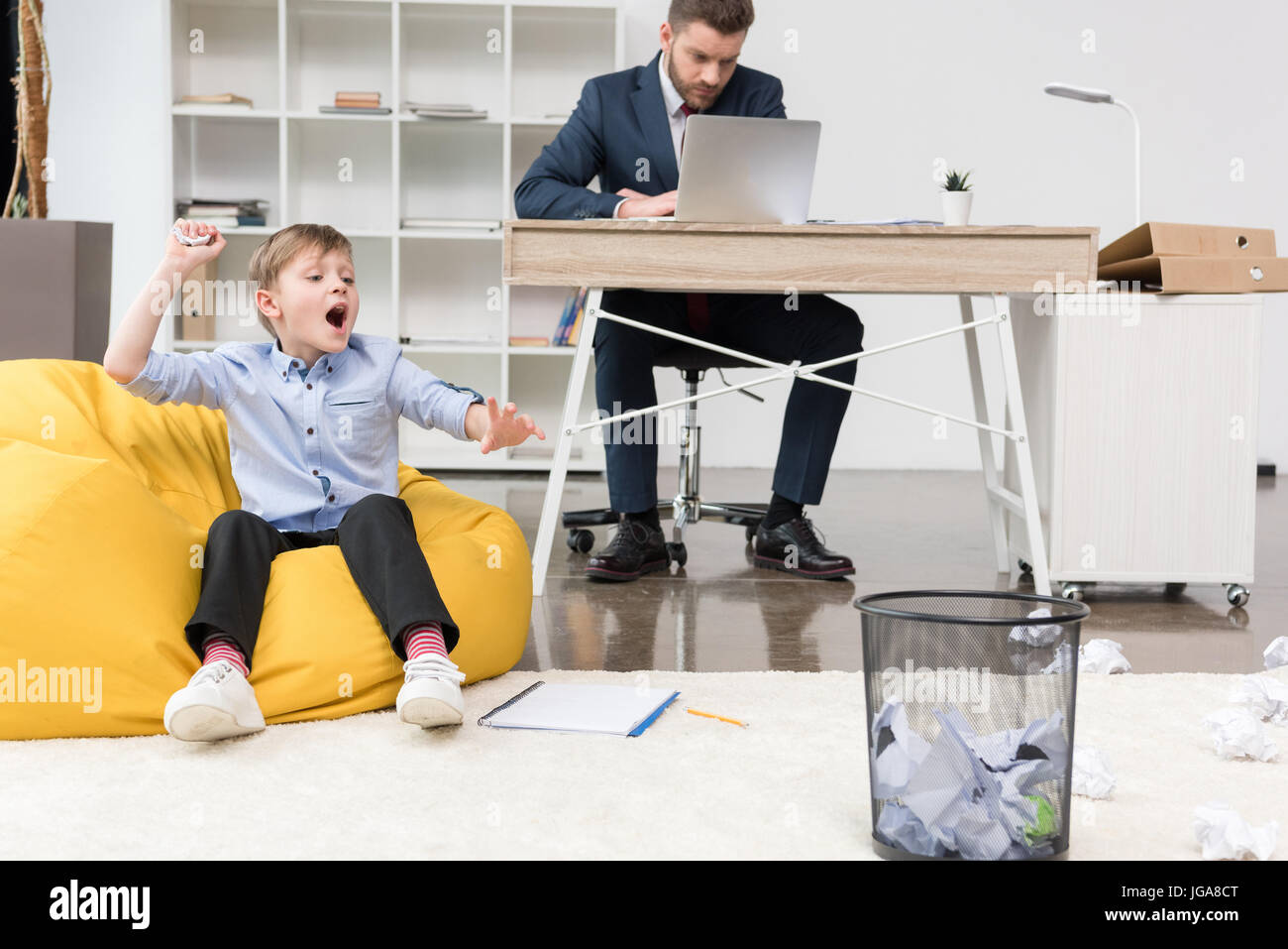 Happy boy playing trashketball while his father working at office Stock ...