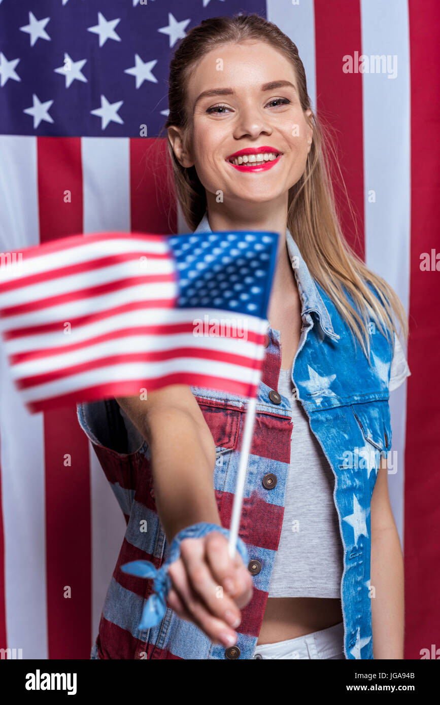 Attractive young woman holding american flag in hand and smiling at ...