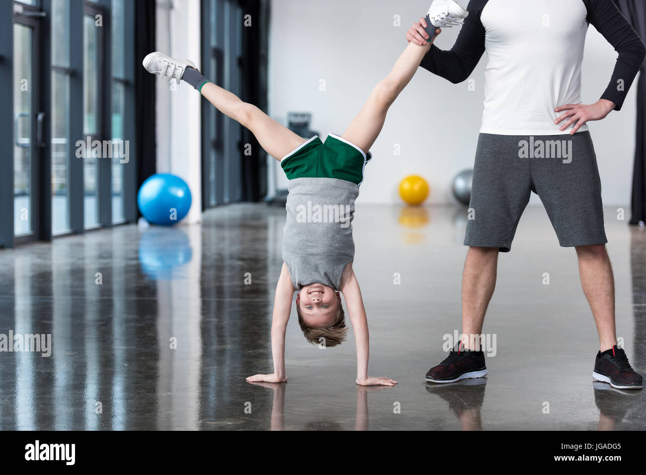 Trainer helping boy standing on hands at exercise room Stock Photo - Alamy