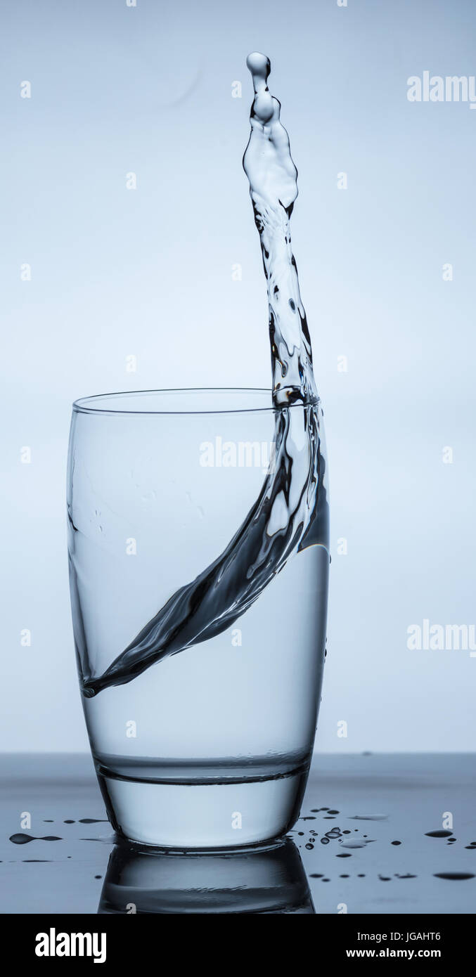water splashing out of a glass on blue background Stock Photo - Alamy