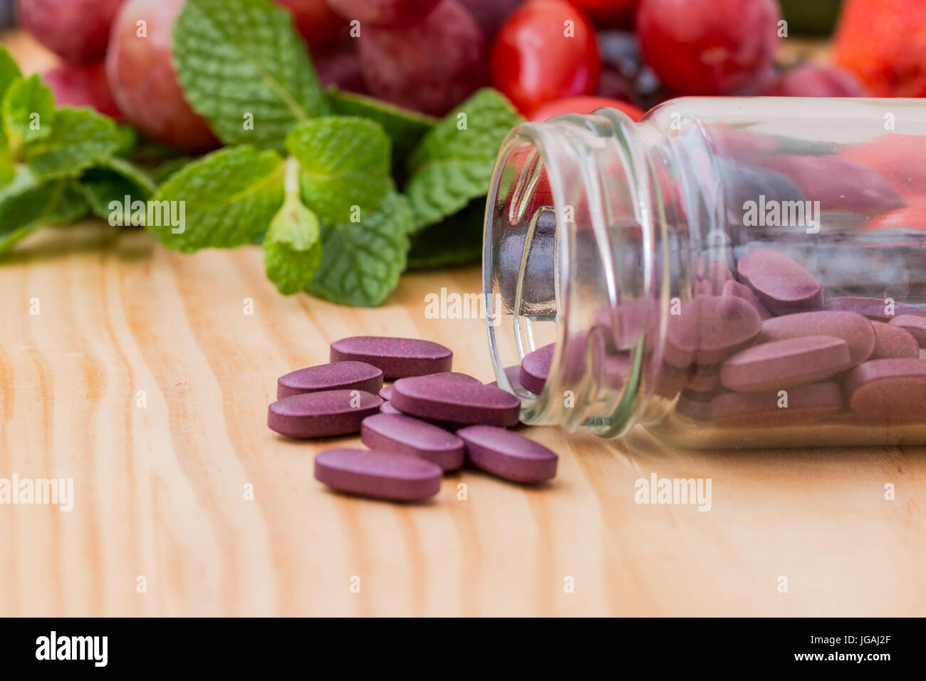 Purple supplements in a bottle and on wooded table with fruit and ...