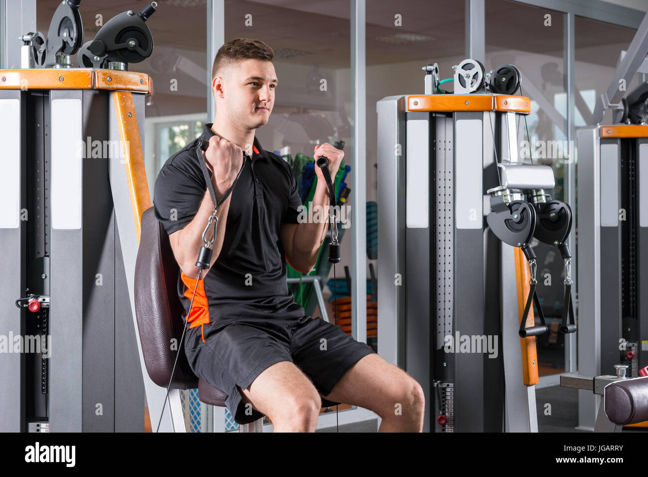 Handsome man training on modern machine and working out in gym room in ...