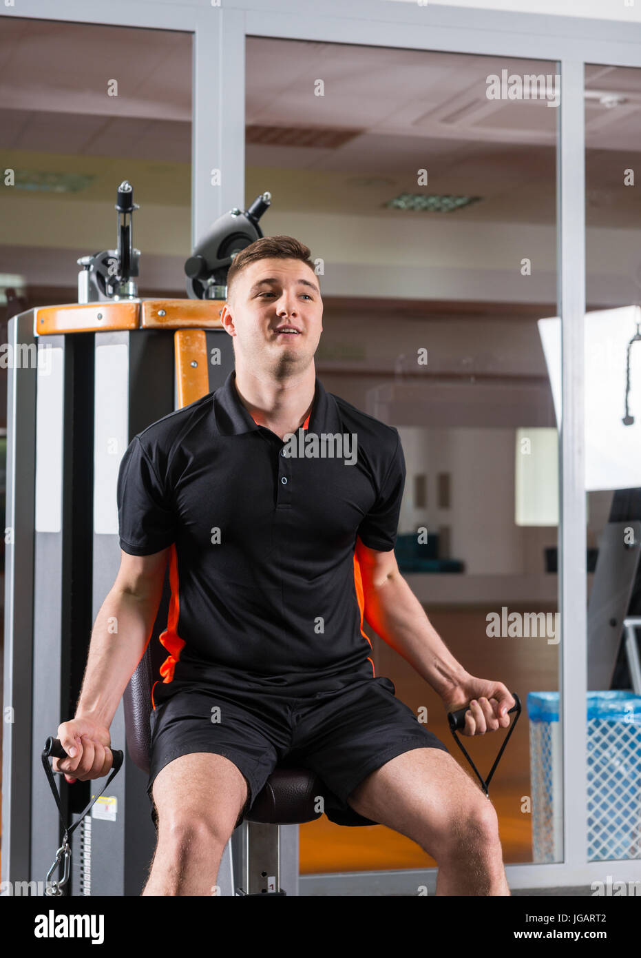 Young handsome man training on modern machine and working out in gym ...