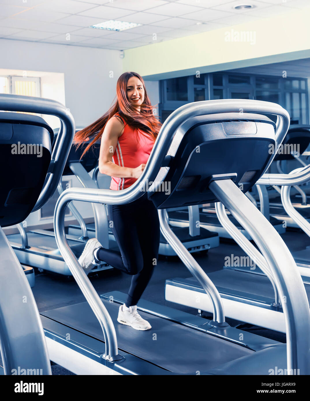 Young happy fit woman running on treadmill at the bright modern gym ...