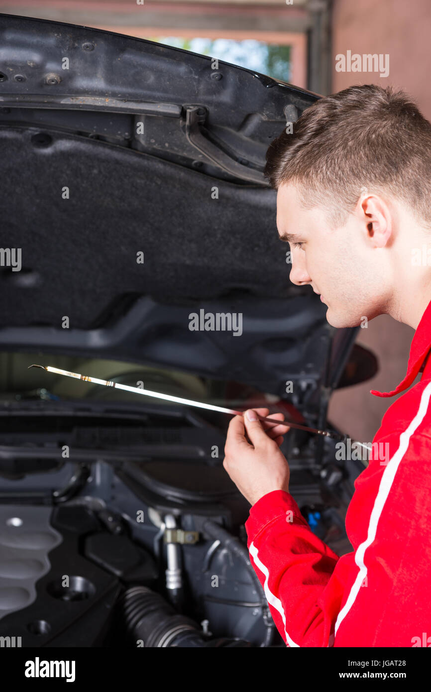 Young male motor mechanic checking the oil level in a car engine ...
