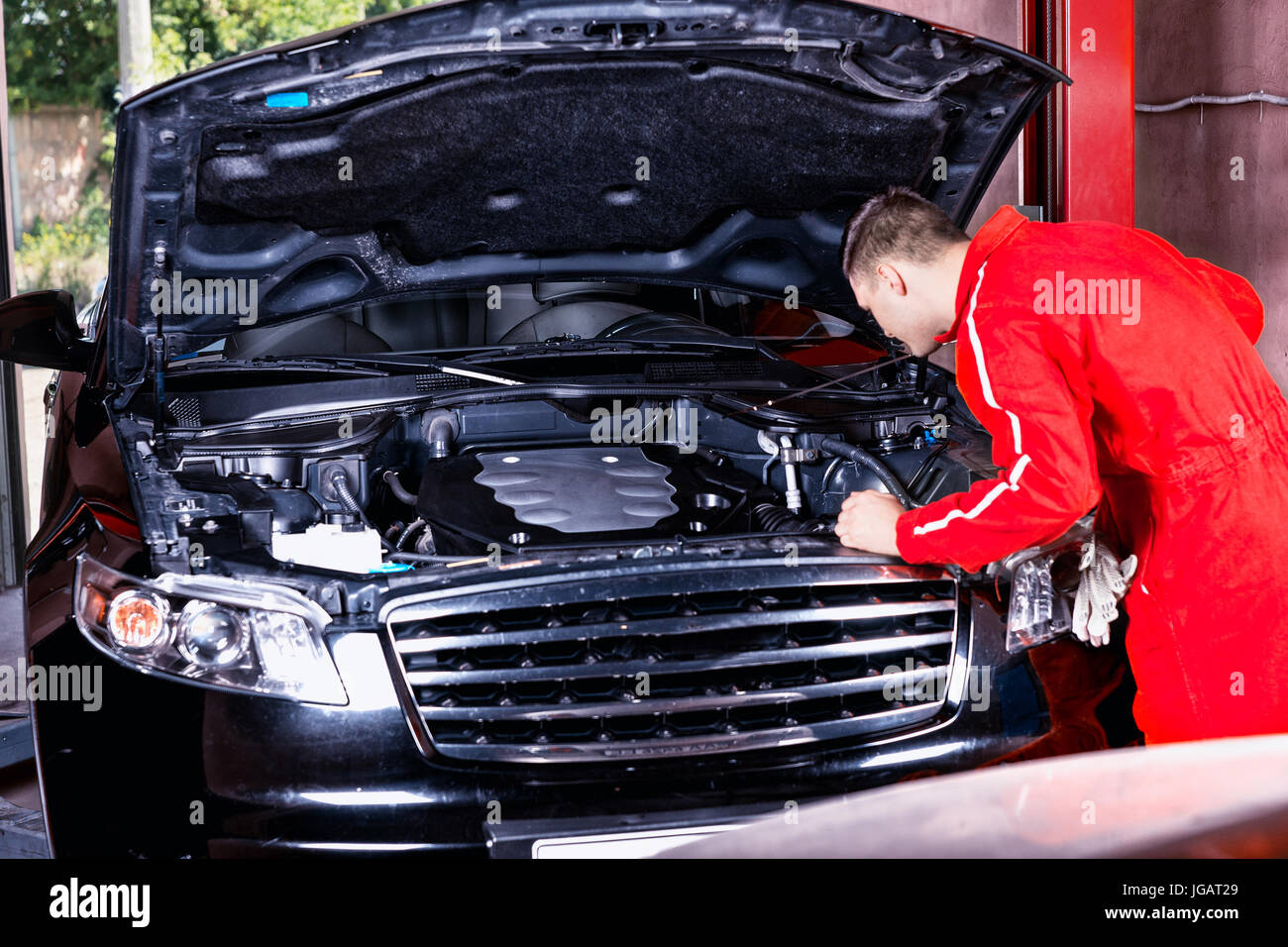 Young male motor mechanic in uniform standing near a black sedan and ...