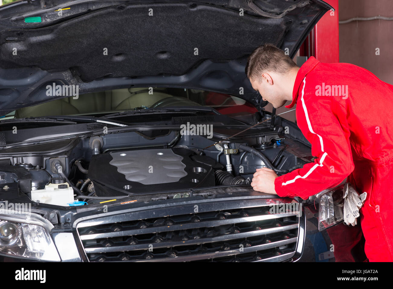 Male motor mechanic in uniform standing near a black sedan and checking ...