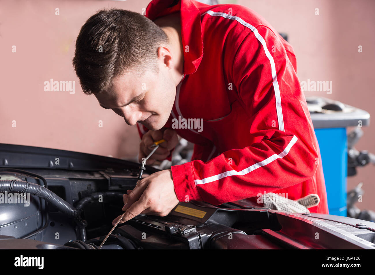 Young mechanic checking the oil level in a car engine holding the ...