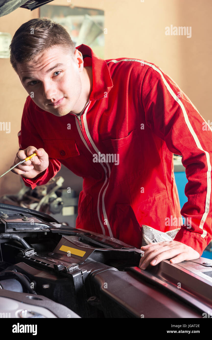 Young handsome mechanic checking the oil level in a car engine holding ...
