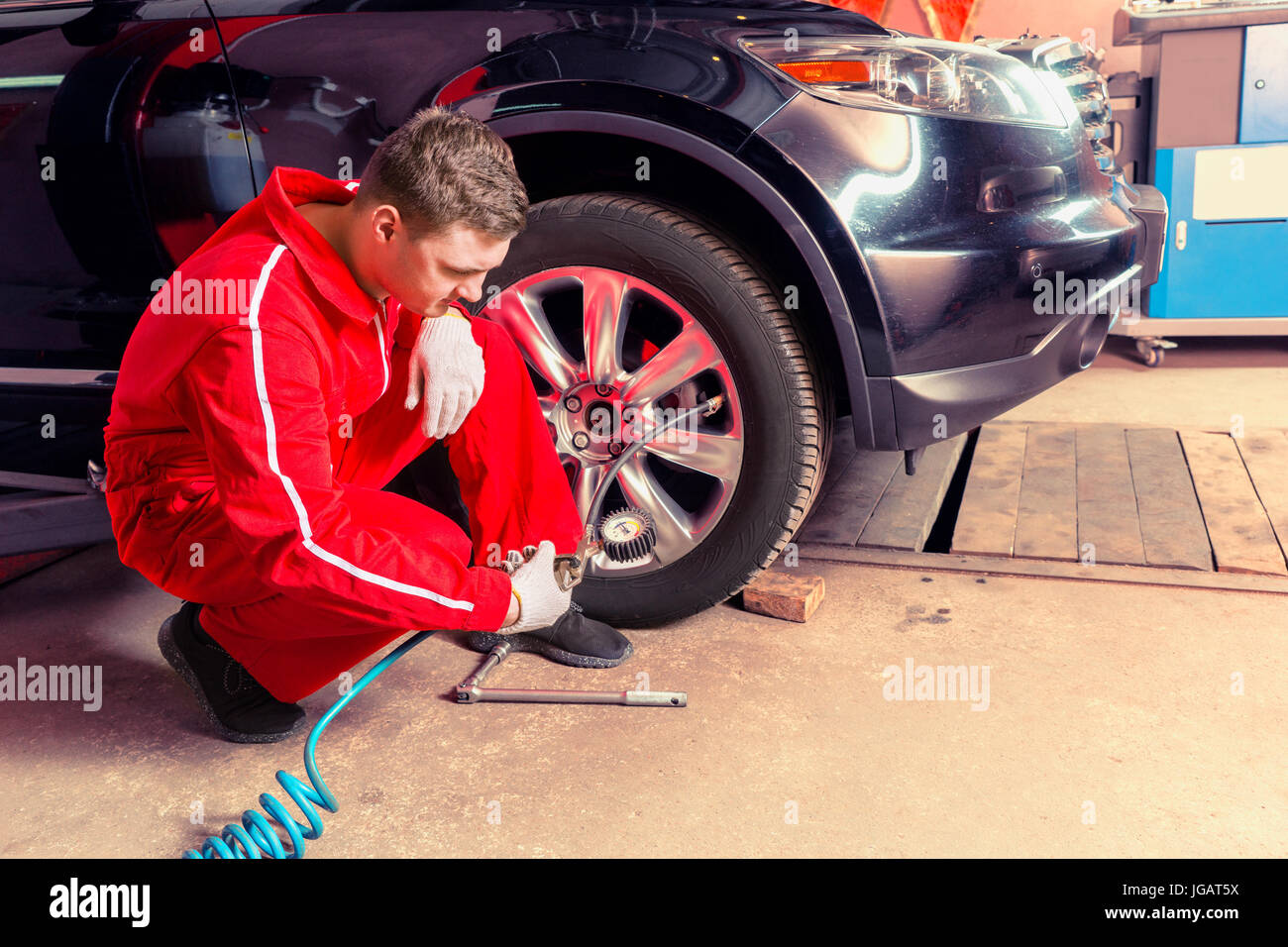 Young male motor mechanic checking the air pressure of a tyre crouching ...
