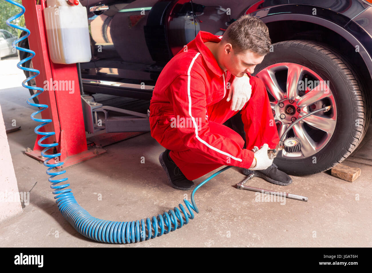Young male auto mechanic checking the air pressure of a tyre crouching ...