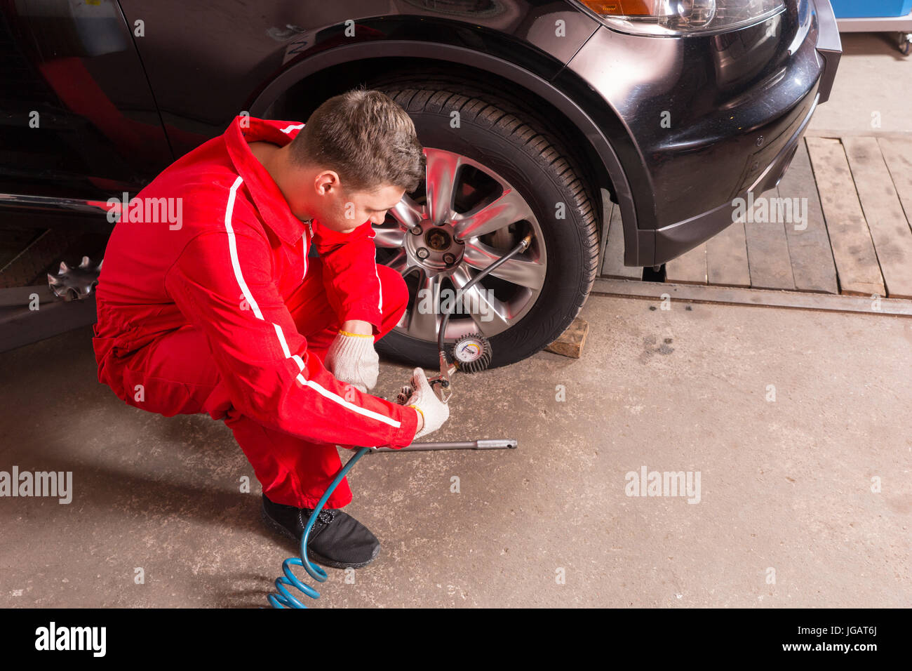 Young auto mechanic checking the air pressure of a tyre crouching down ...