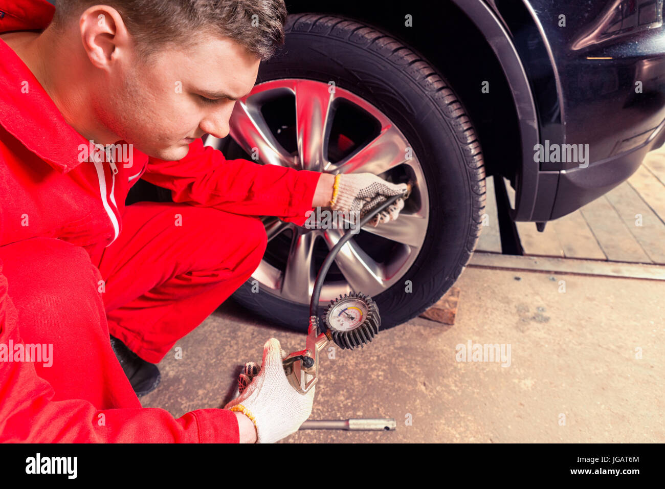 Young motor mechanic checking the air pressure of a tyre crouching down ...