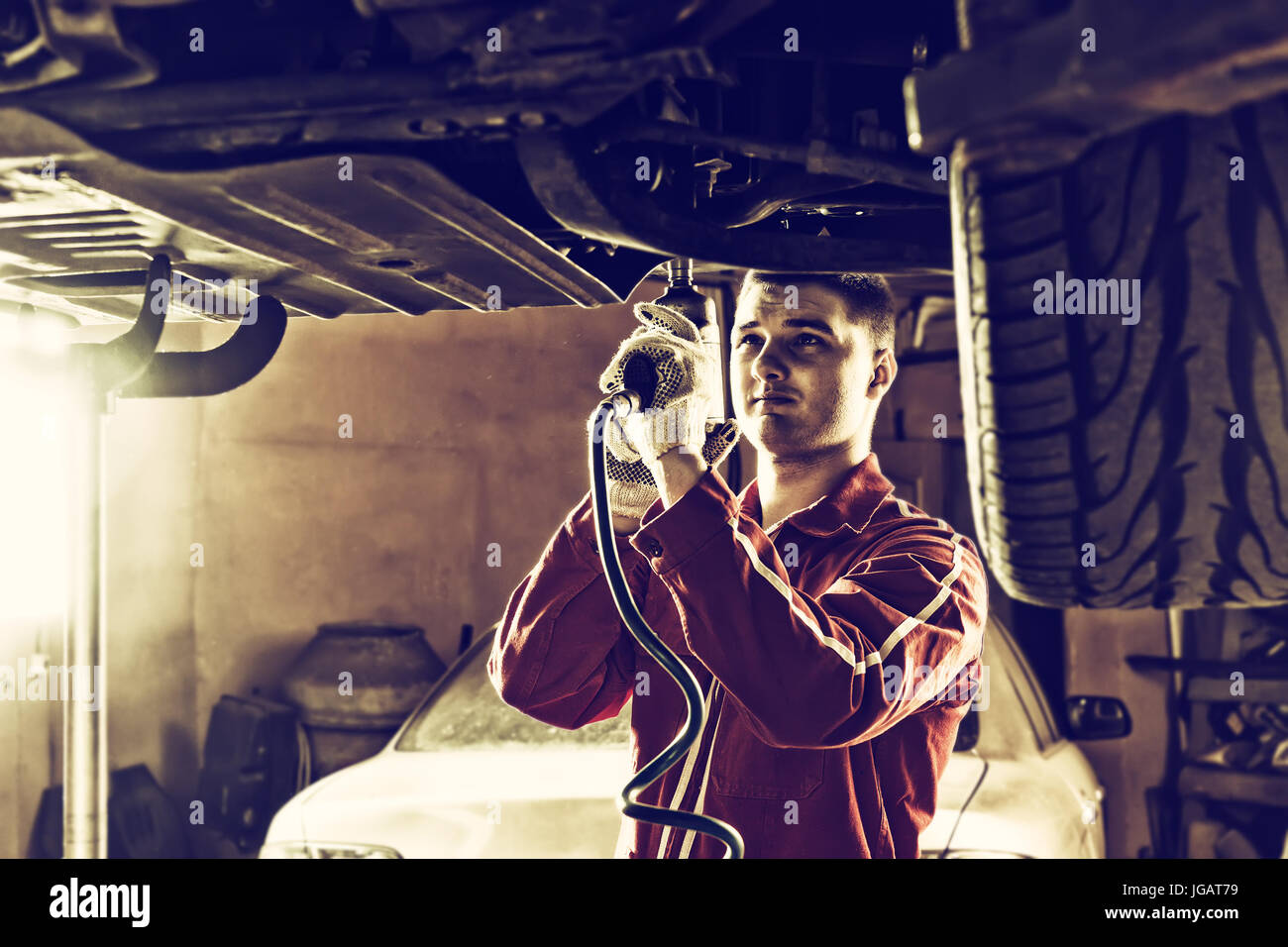 Professional handsome male auto mechanic in uniform working underneath ...