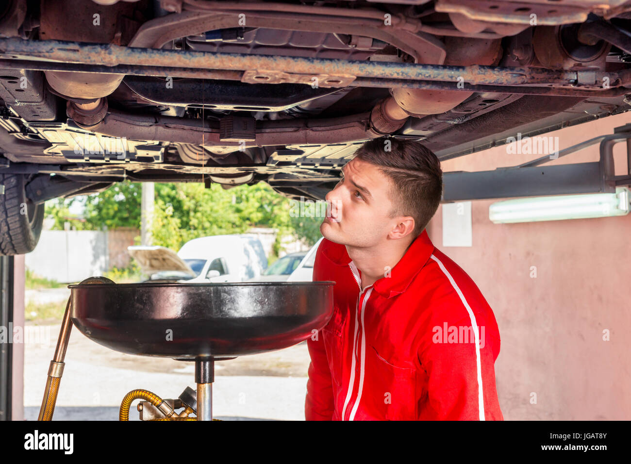 Young auto mechanic in uniform watching how oil jet flows out into ...