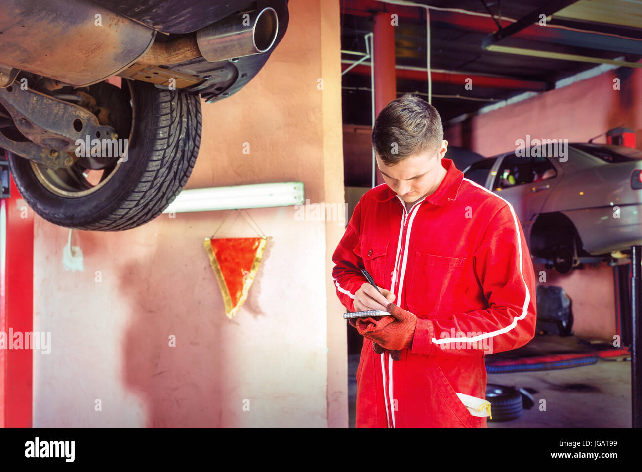 Young male motor mechanic standing making notes underneath a lifted car ...