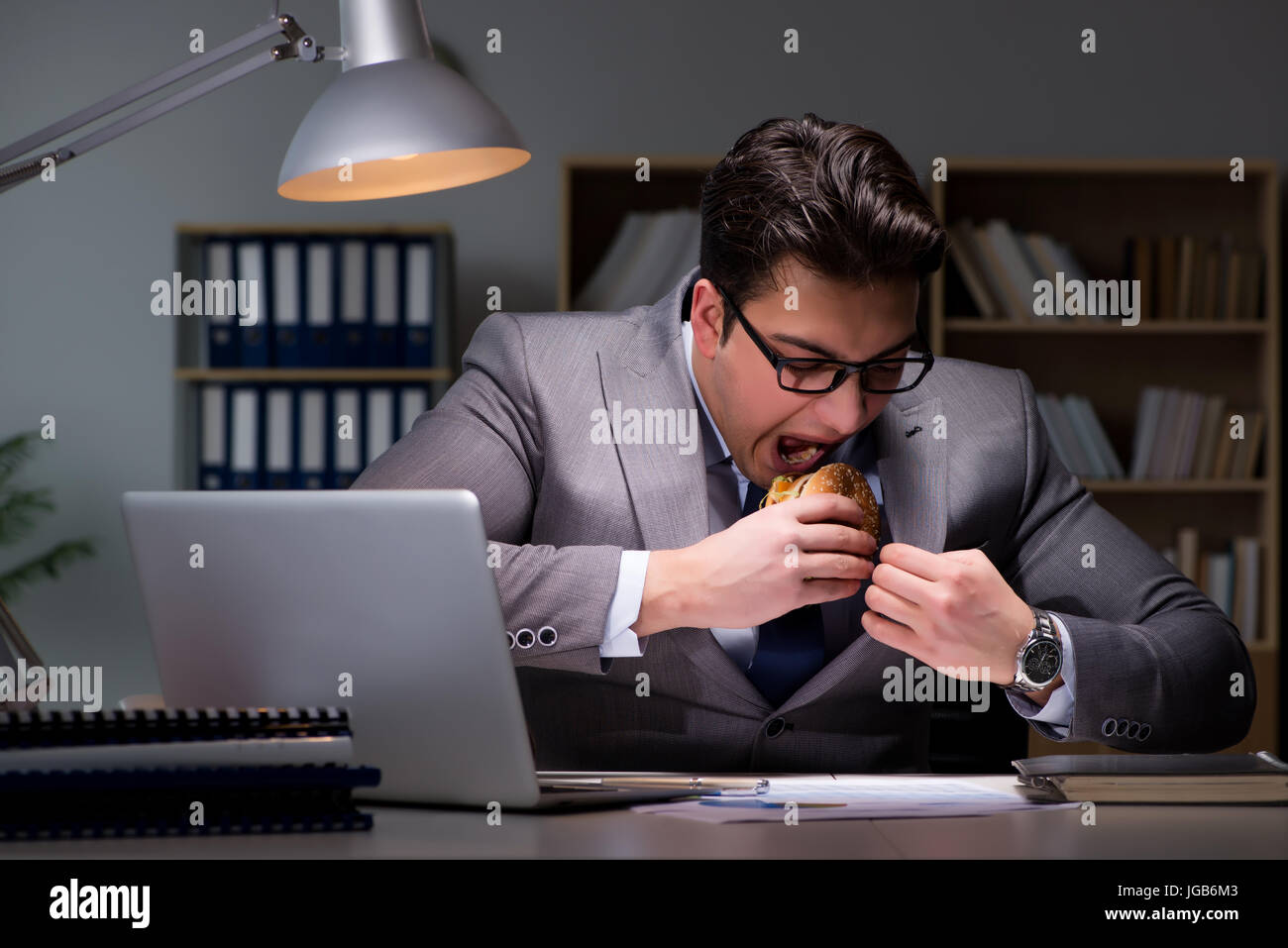 Businessman late at night eating a burger Stock Photo - Alamy