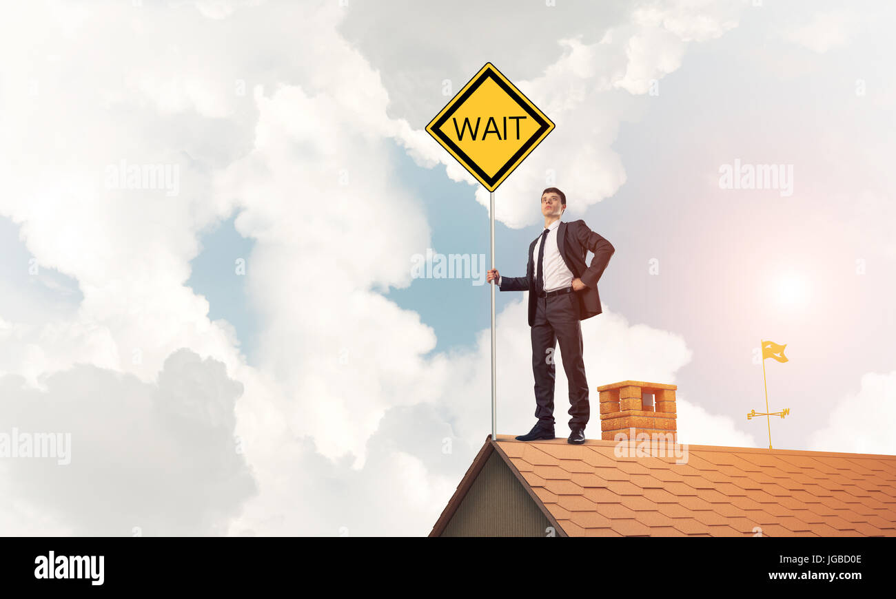 Young businessman on house brick roof holding yellow signboard Stock ...