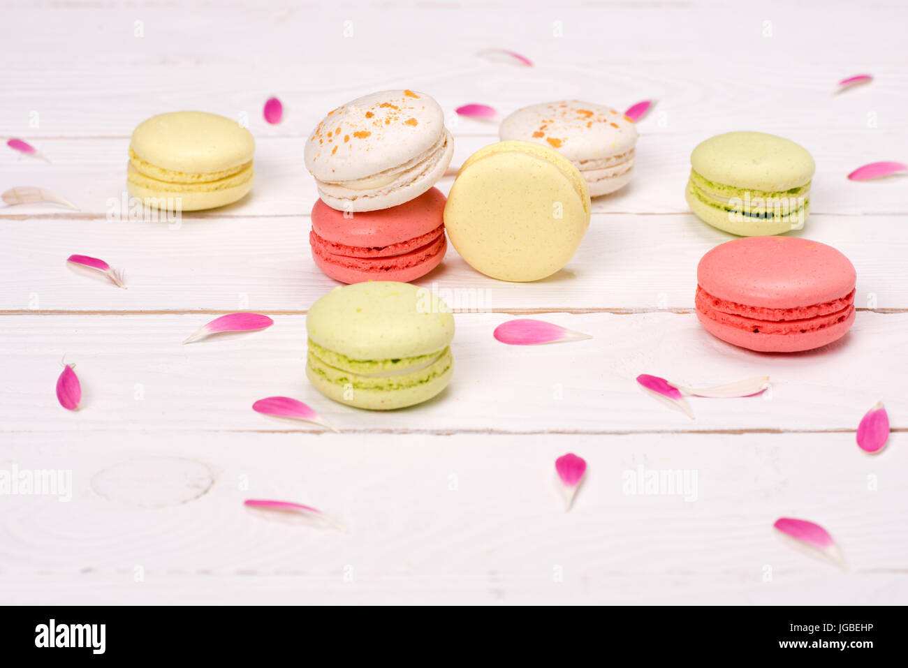 Still life of fresh macarons on the table with pink petals. sweets ...