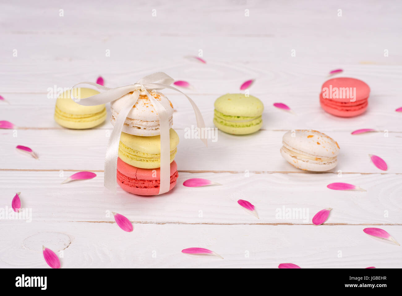 Still life of fresh macarons on the table with pink petals. sweets ...