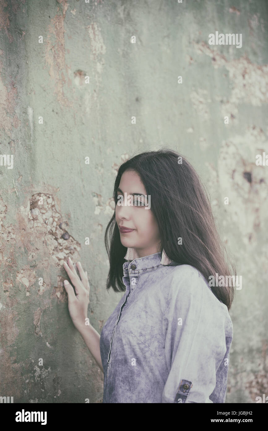Beautiful young woman leaning against the wall looking away thinking ...