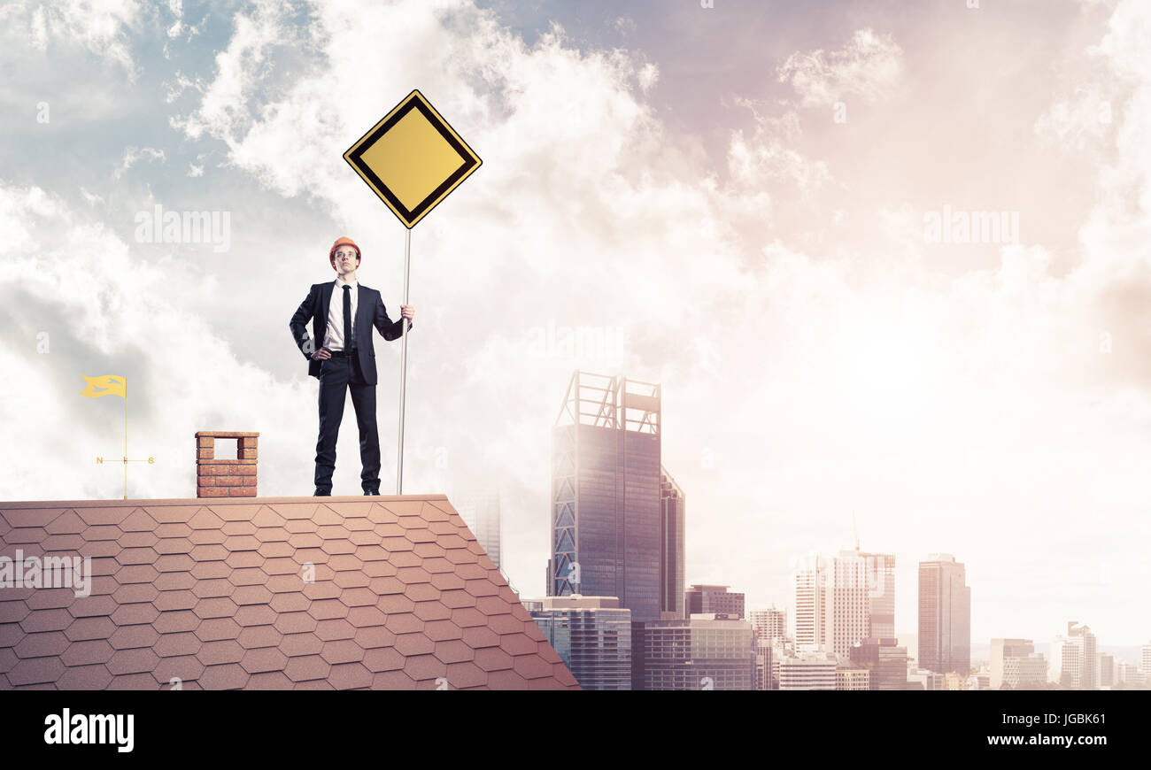 Young businessman on house brick roof holding yellow signboard a Stock ...