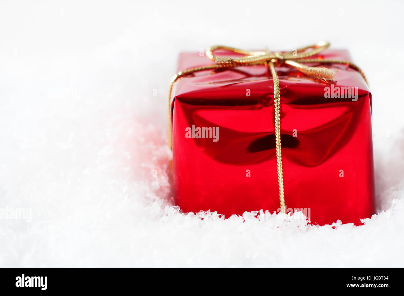 A single Christmas gift box in shiny red foil wrapping and tied to a ...