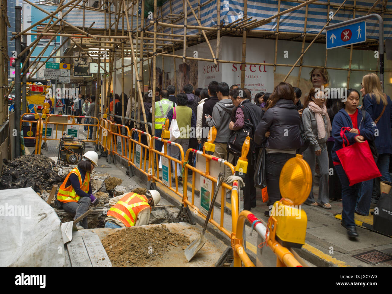 Pedestrians on crowded pavement walking under bamboo scaffolding and ...