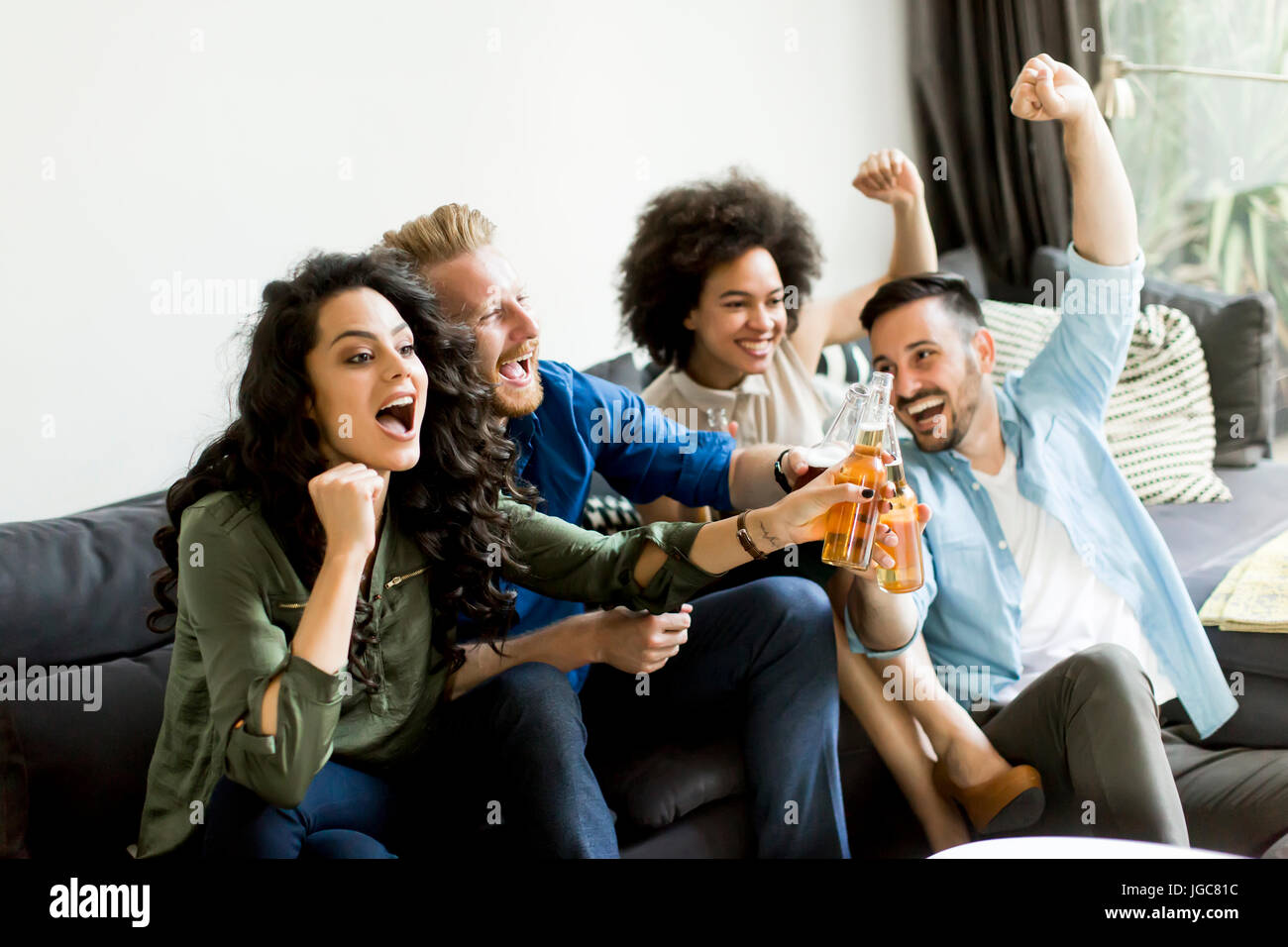 Group of friends watching TV , drinking cider and having fun in the ...