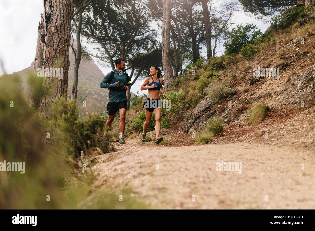 Full length portrait of young man and woman running on country path ...