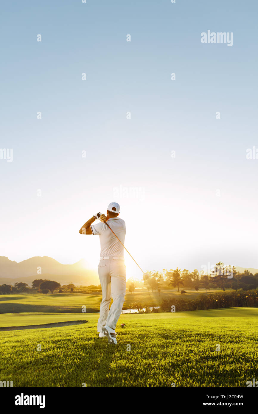 Rear view of golfer hitting driver on a golf course in the sun. Full ...