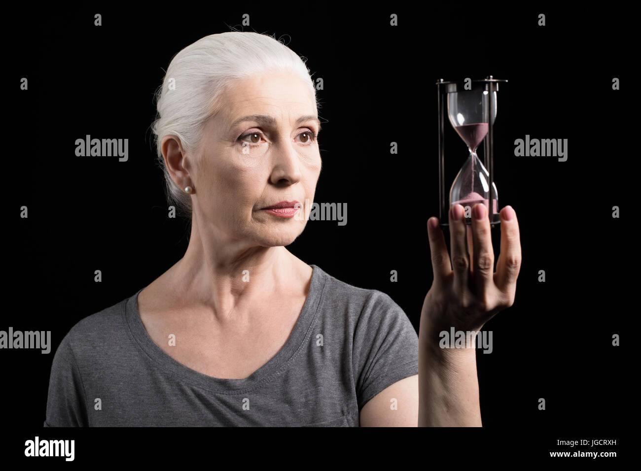 senior woman holding sand clock isolated on black Stock Photo - Alamy