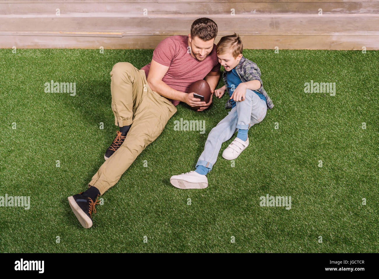 father with ball and little son laying on the grass at backyard, dad ...