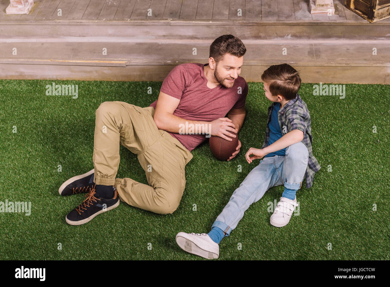 father with ball and little son laying on the grass at backyard, dad ...