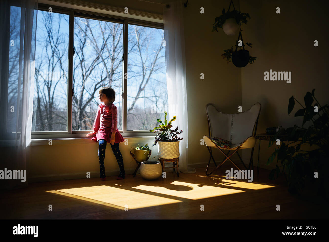 Girl sitting in sunlight looking through a window Stock Photo - Alamy