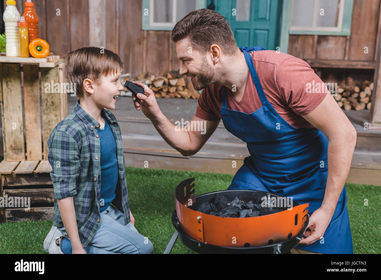 side view of smiling father and son preparing grill for barbecue Stock ...